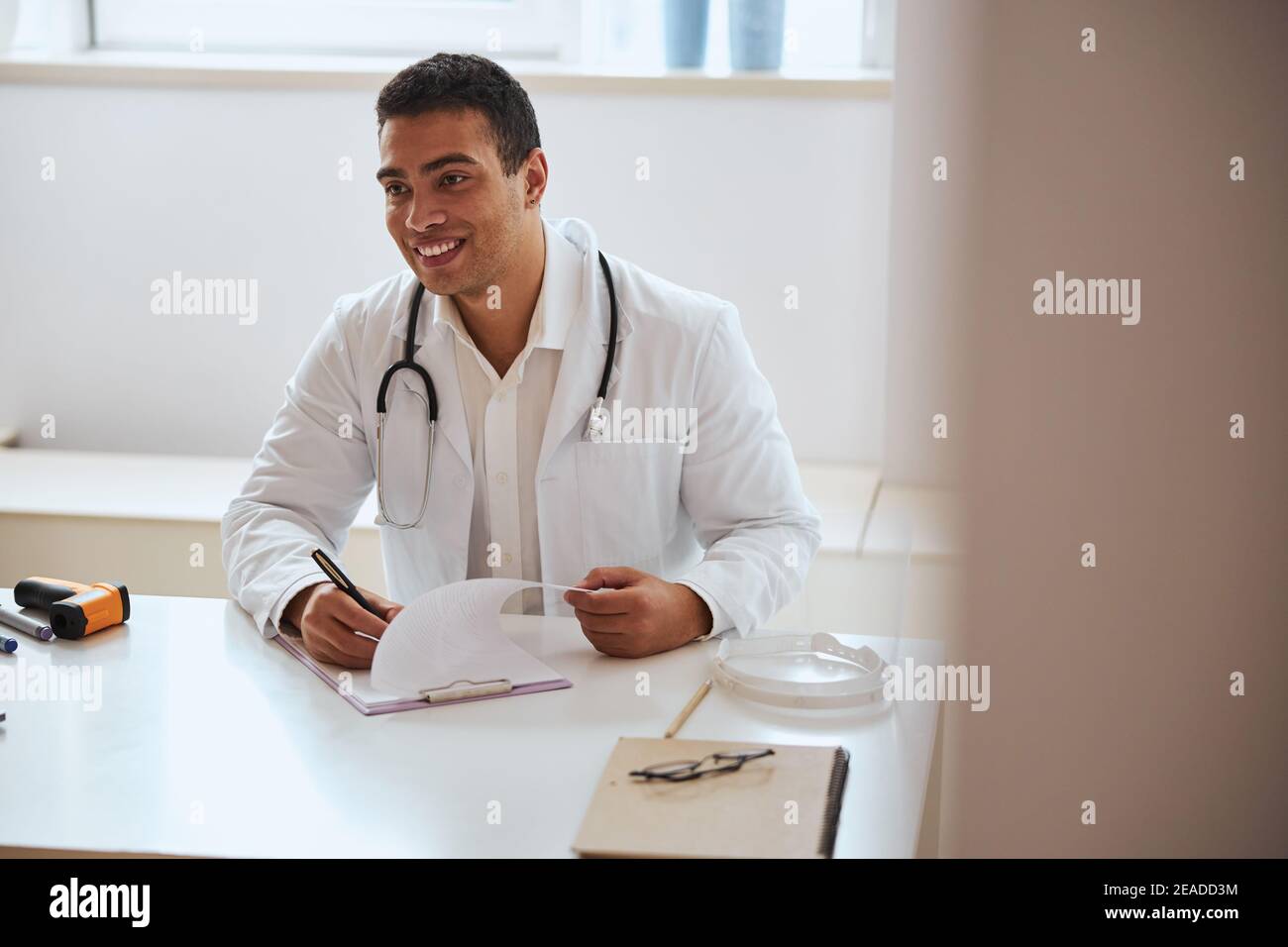 Happy smiling doctor sitting at the desk in room indoors Stock Photo ...