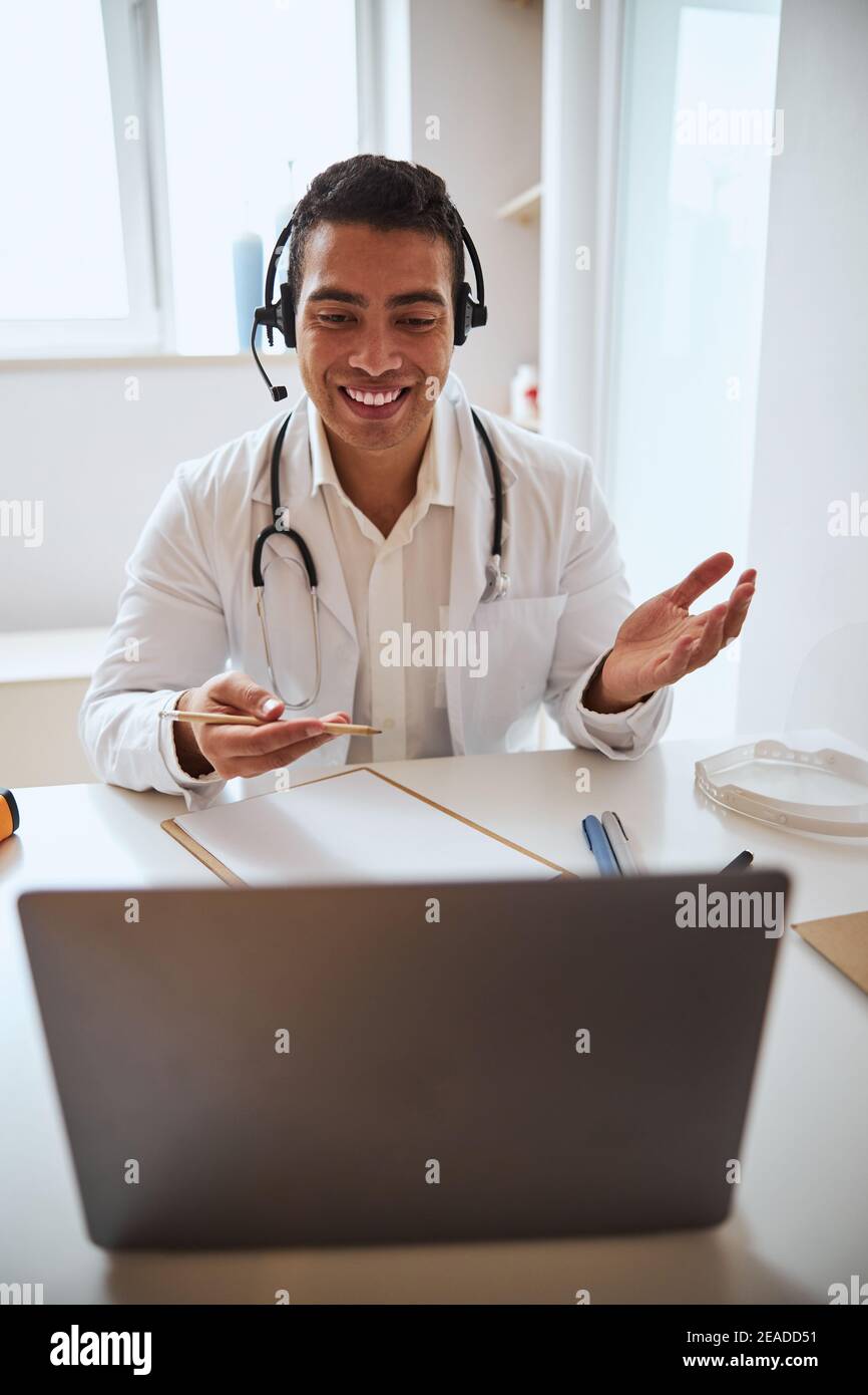 Happy positive energetic mad doctor with stethoscope working online ...