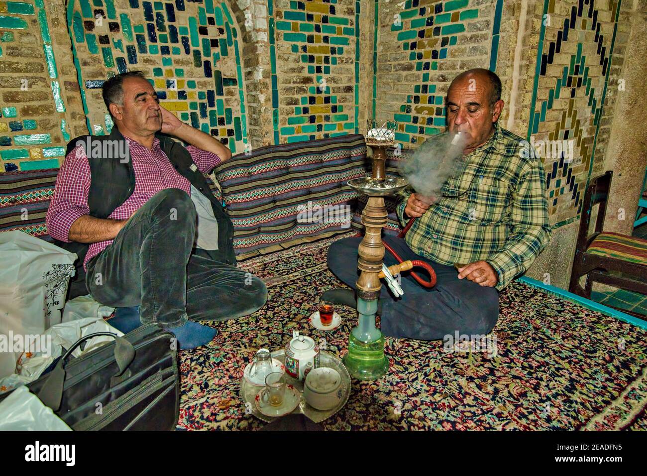 Two men smoking shisha from a hookah while drinking tea at a teahouse ...