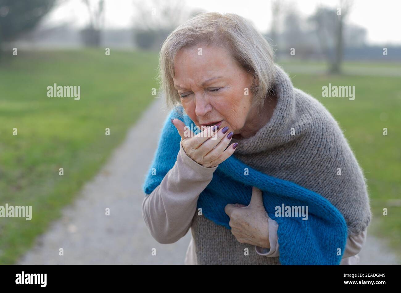 Elegant senior woman coughing into her hand while clutching her chest ...