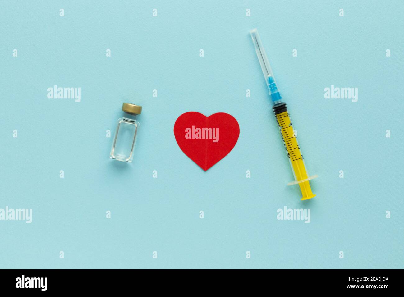 Syringe, glass vial with liquid and red paper heart on blue background ...