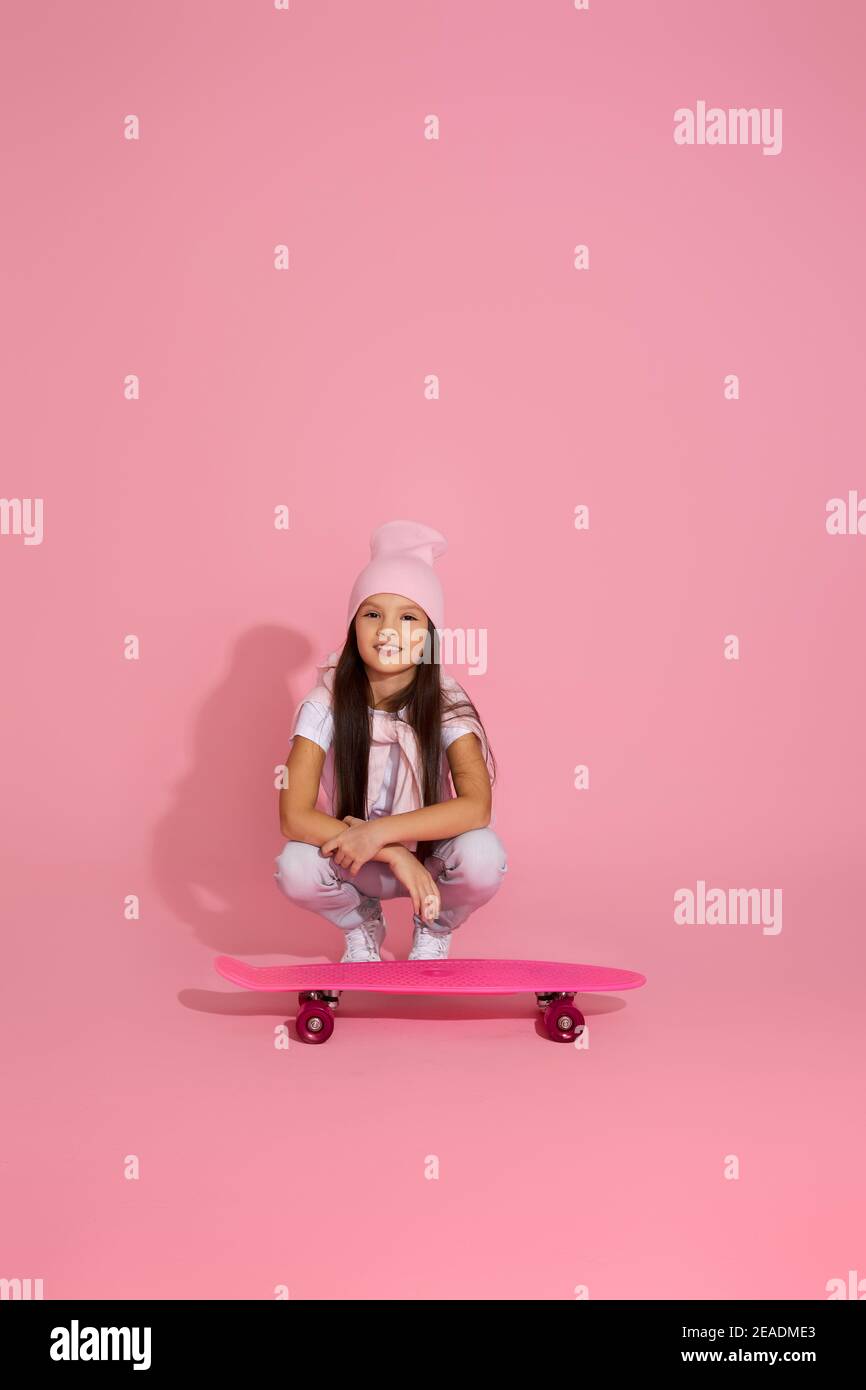 cool little child girl with pink skateboard in casual clothes on pink ...
