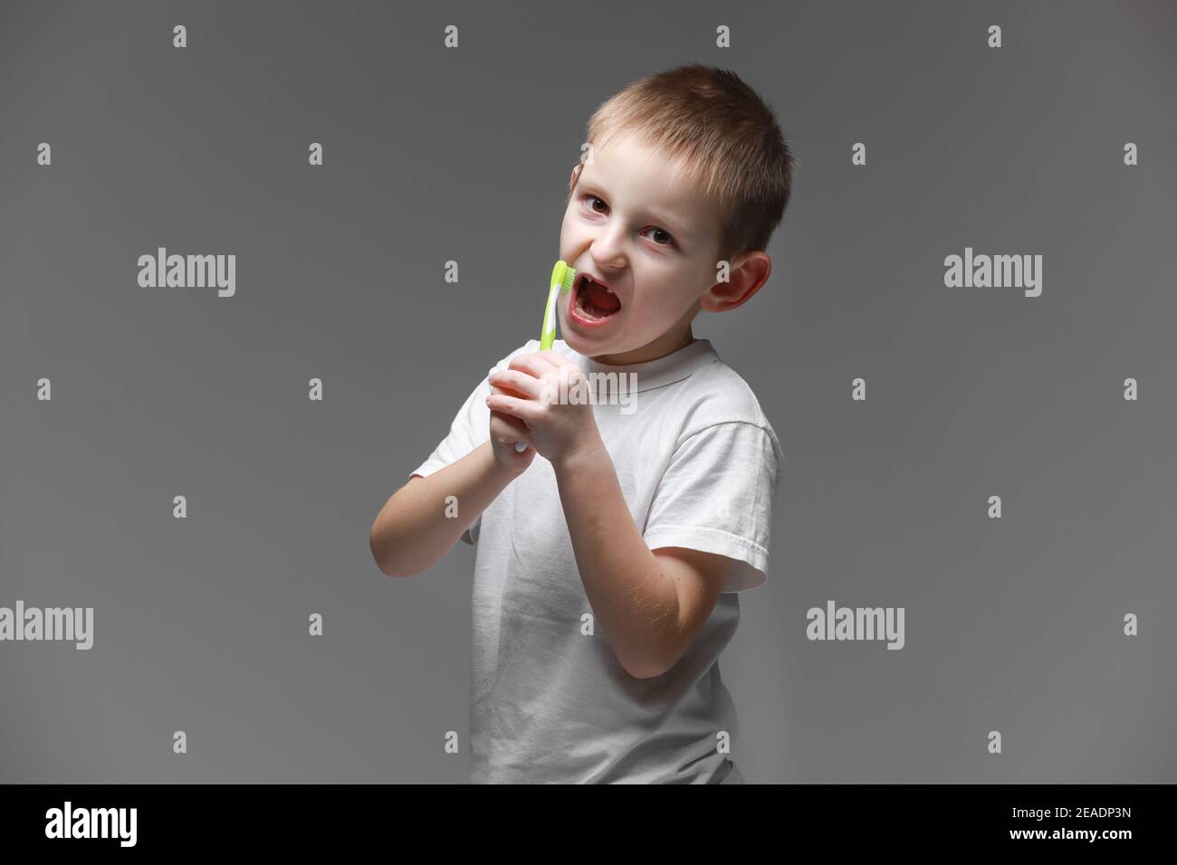 Happy child kid boy brushing teeth with toothbrush on gray background ...