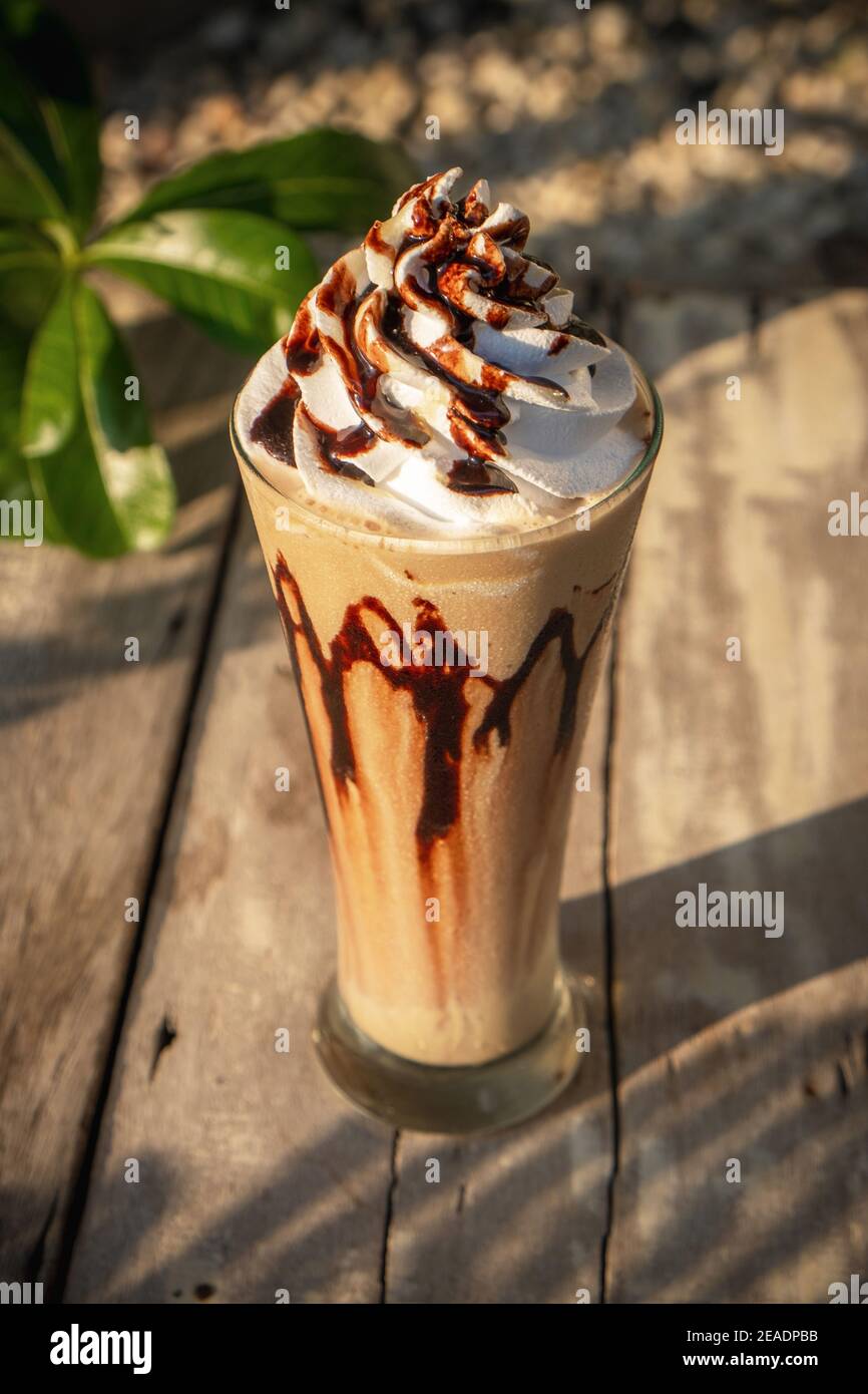 Coffee frappe with whipped cream on old wooden table in the morning sun ...