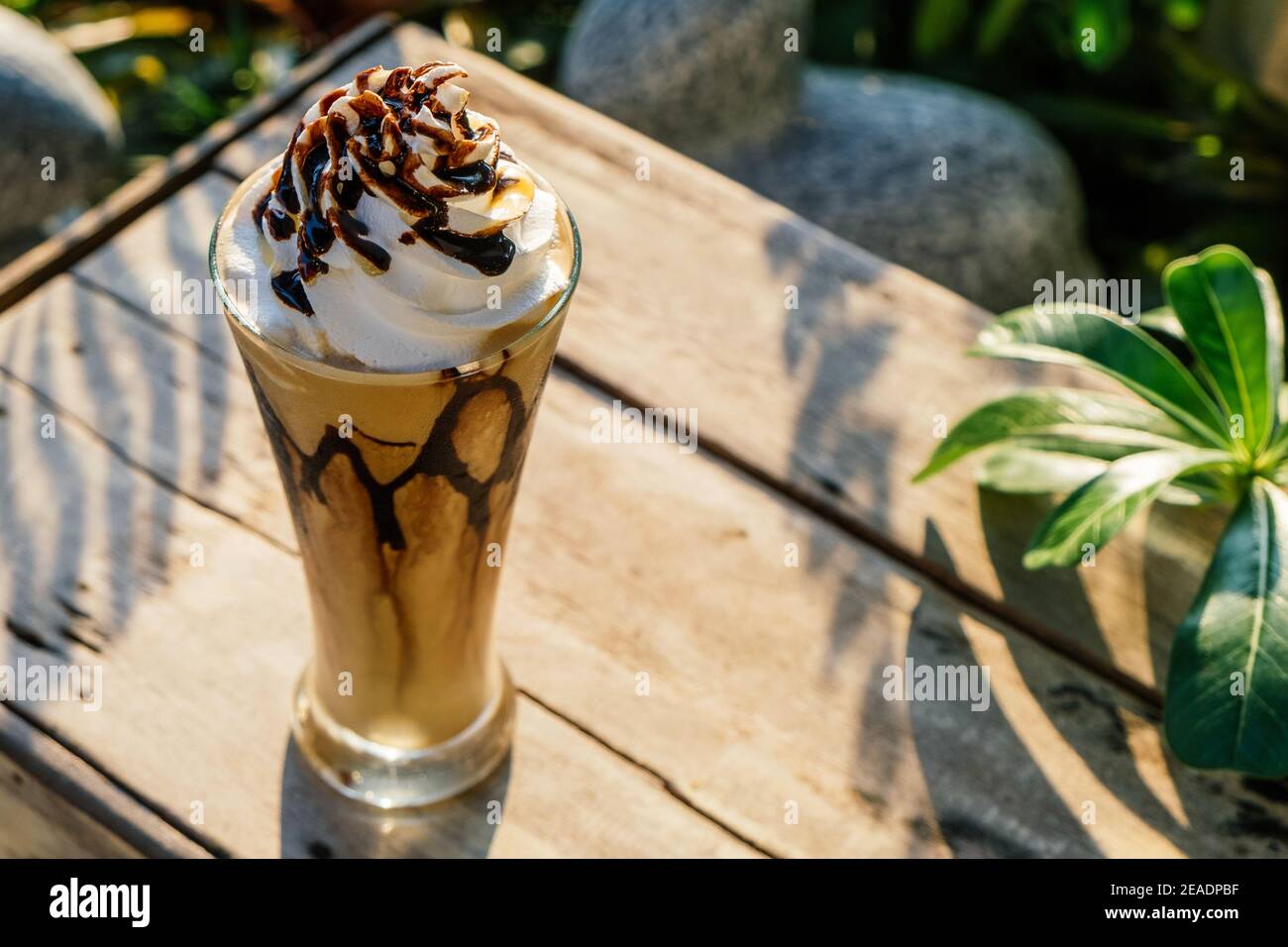 Coffee frappe with whipped cream on old wooden table in the morning sun ...