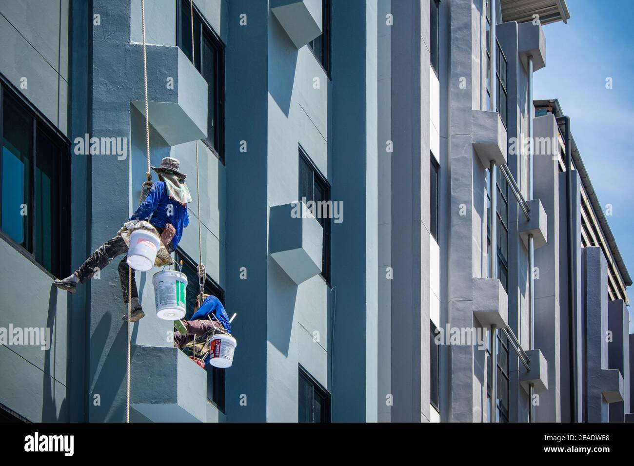 2 painters are hanging on ropes and harnesses paint the exterior of ...