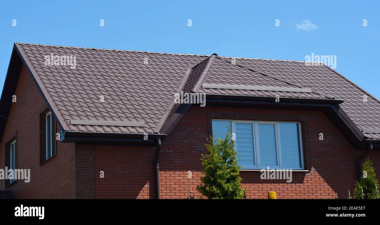 A close-up on a brown attic mansard metal tiled roof with snow guards ...
