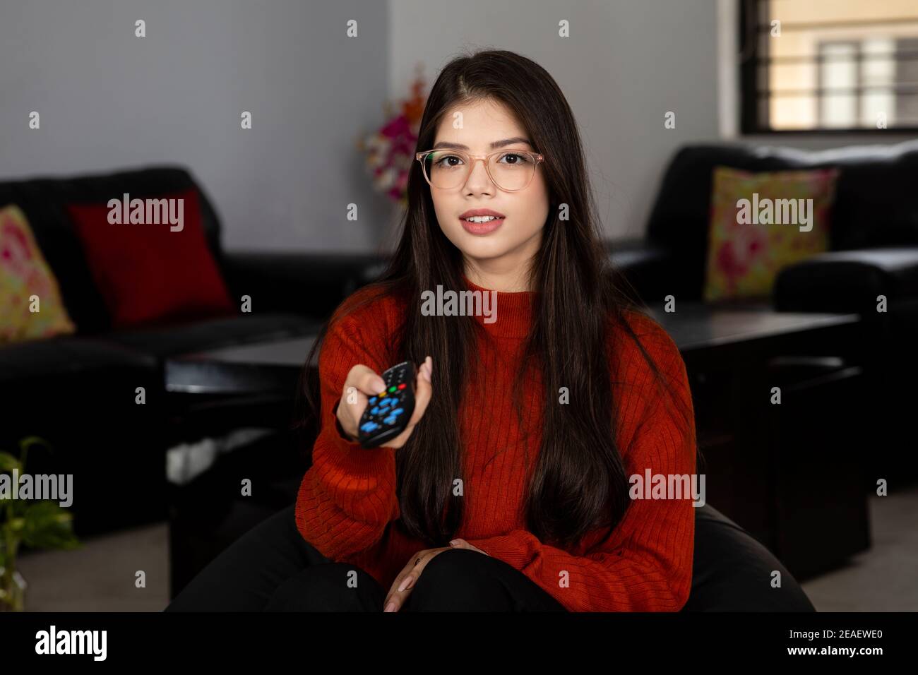 Pretty young woman holding TV remote control in her hands sitting in ...