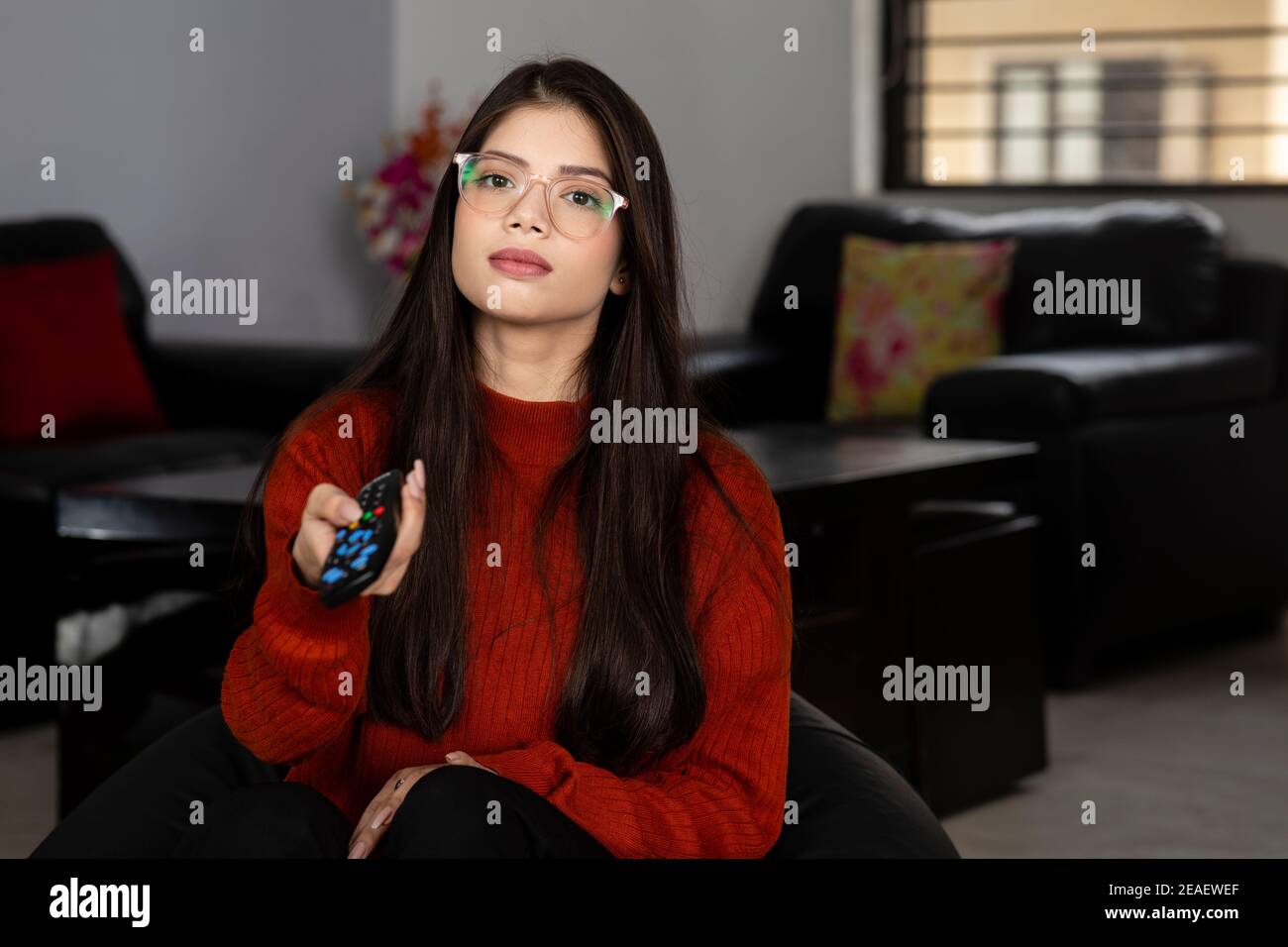 Pretty young woman holding TV remote control in her hands sitting in ...