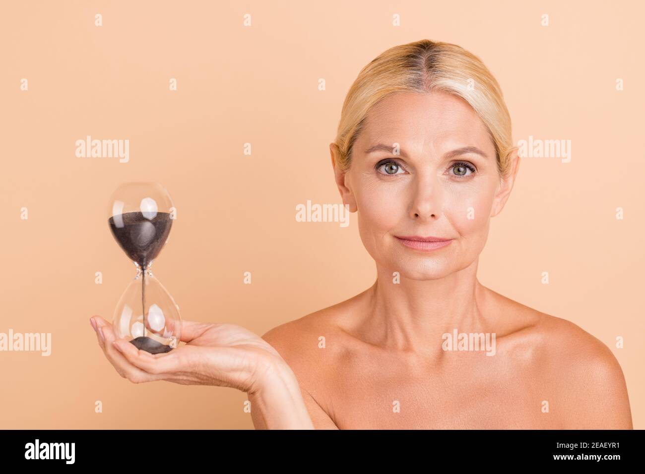 Portrait of attractive middle aged woman hold hourglass clock skin care ...