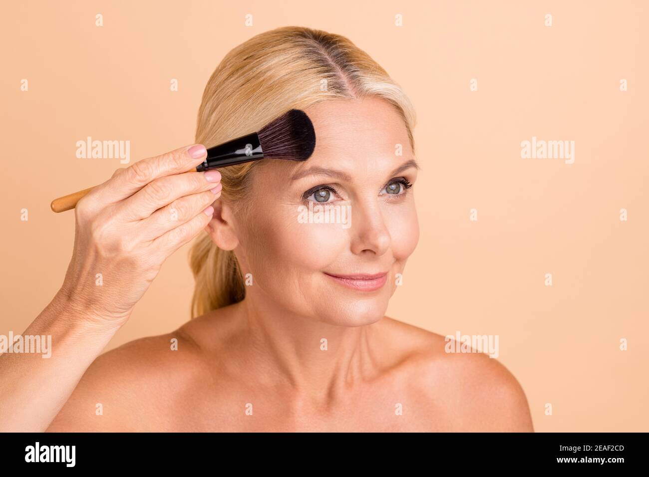 Close-up portrait of lovely middle aged lady applying natural powder ...