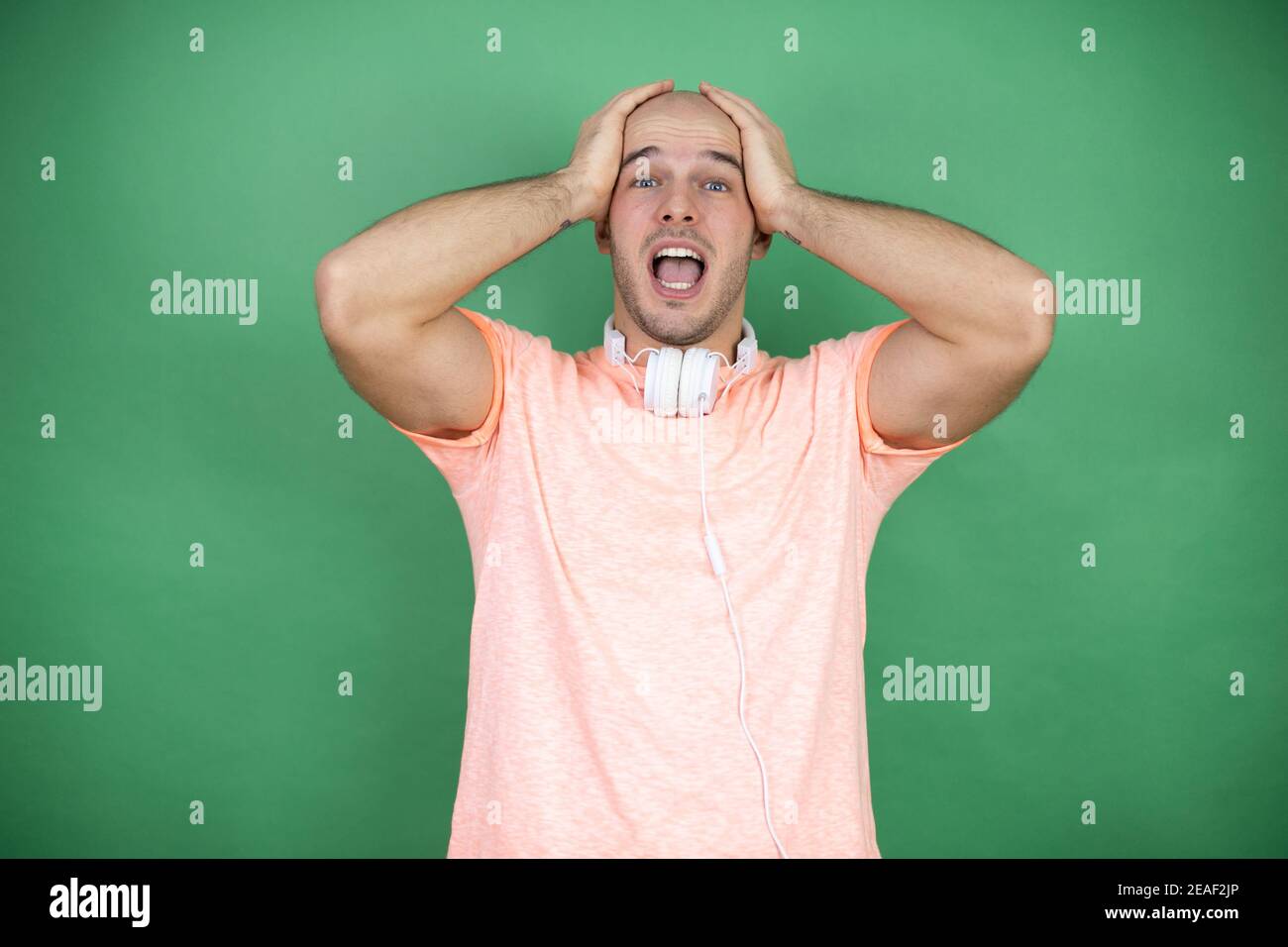 Young bald man using headphones over green background crazy and scared ...