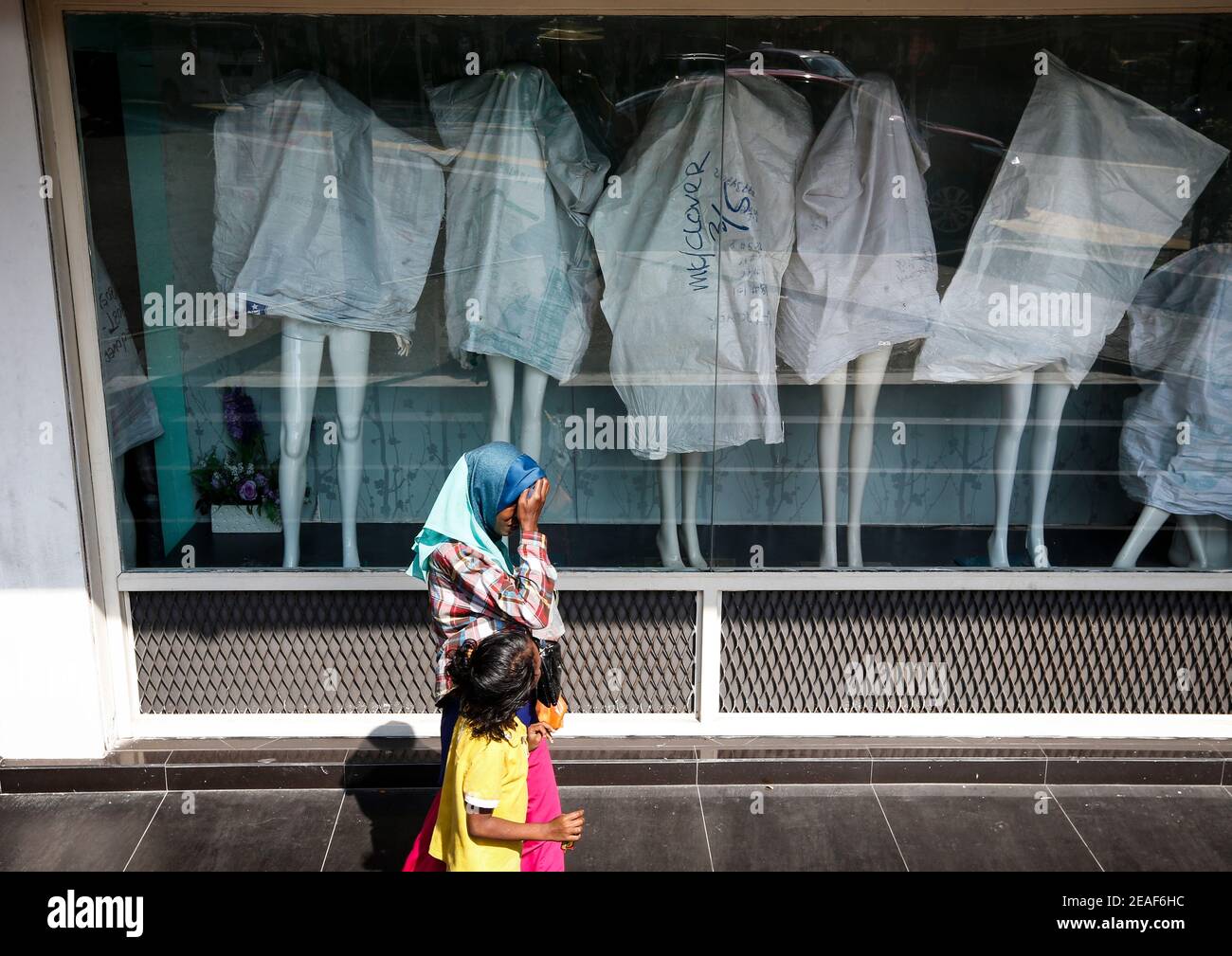 A Muslim woman and her child walk past a closed Whitney Cover fashion ...
