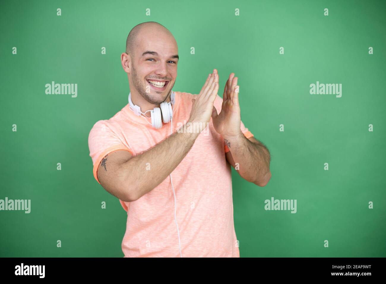 Young bald man using headphones over green background clapping and ...
