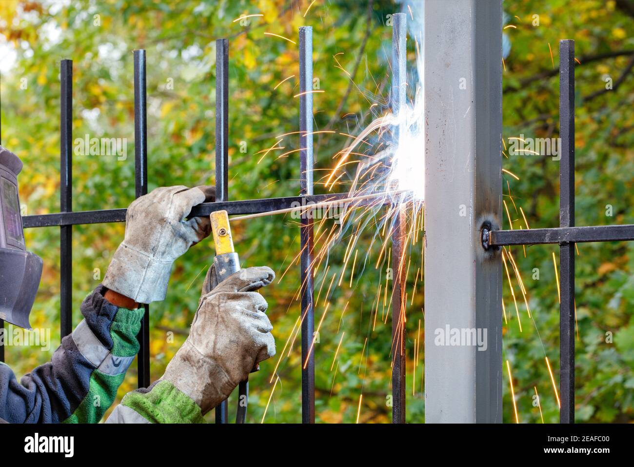 A welder in a safety helmet and gloves welds an iron grate to a metal ...