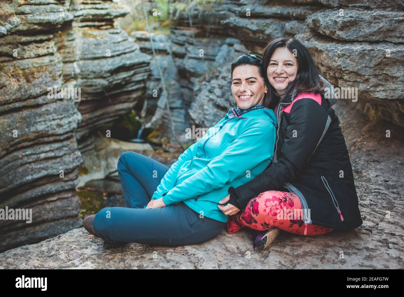Two women hikers, smiling and hugging. Sedimentary rocks in the ...