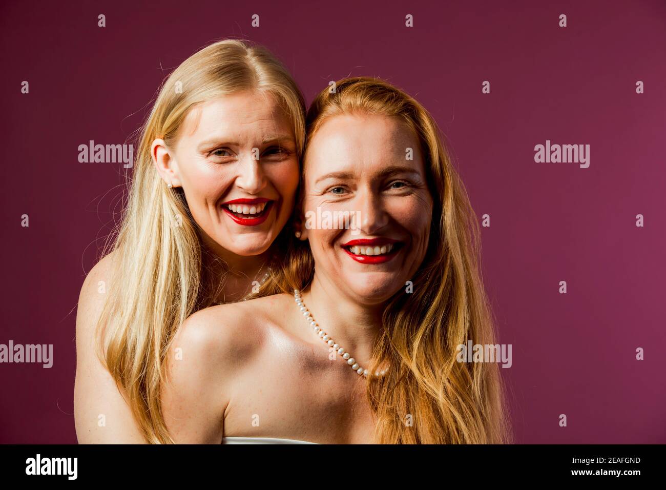 Two pretty sisters hugging on purple background Stock Photo - Alamy