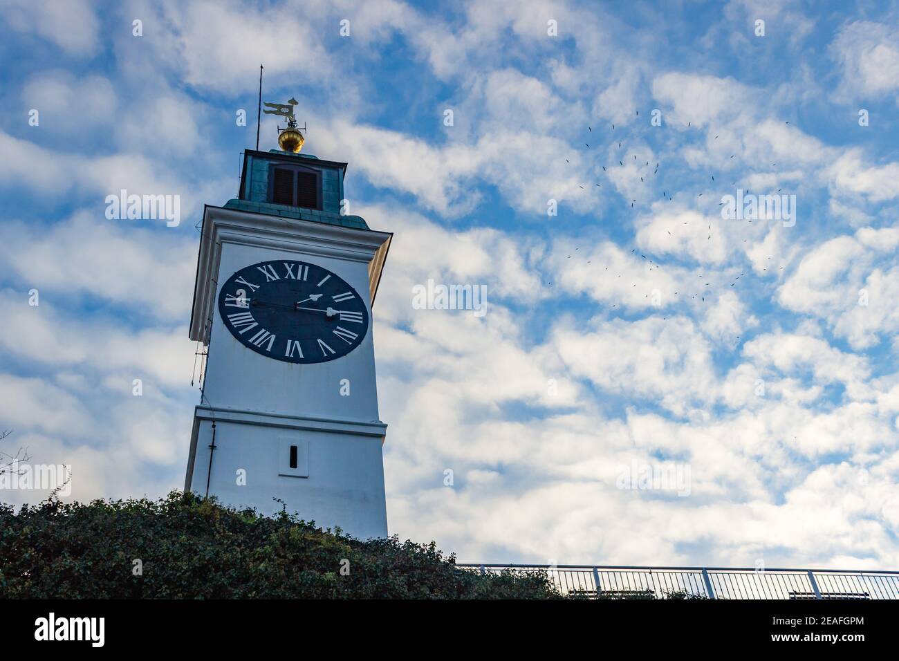 Low angle shot of a white tower with a big wall clock behind the fence ...