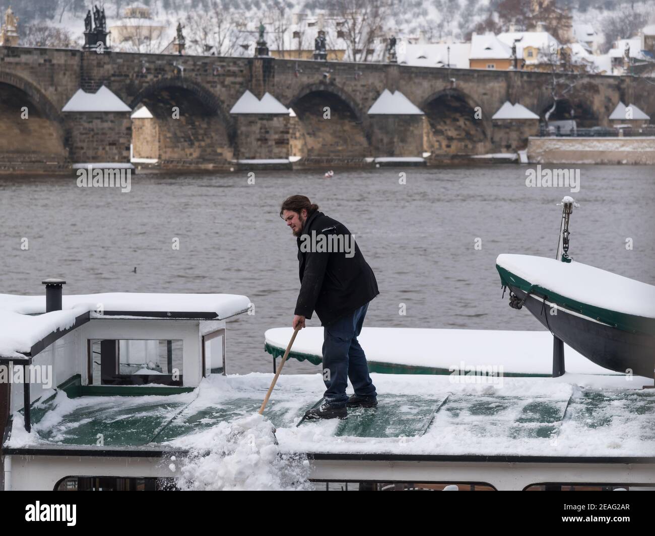 A man sweeps snow off the roof of a cruise ship on the Vltava river ...