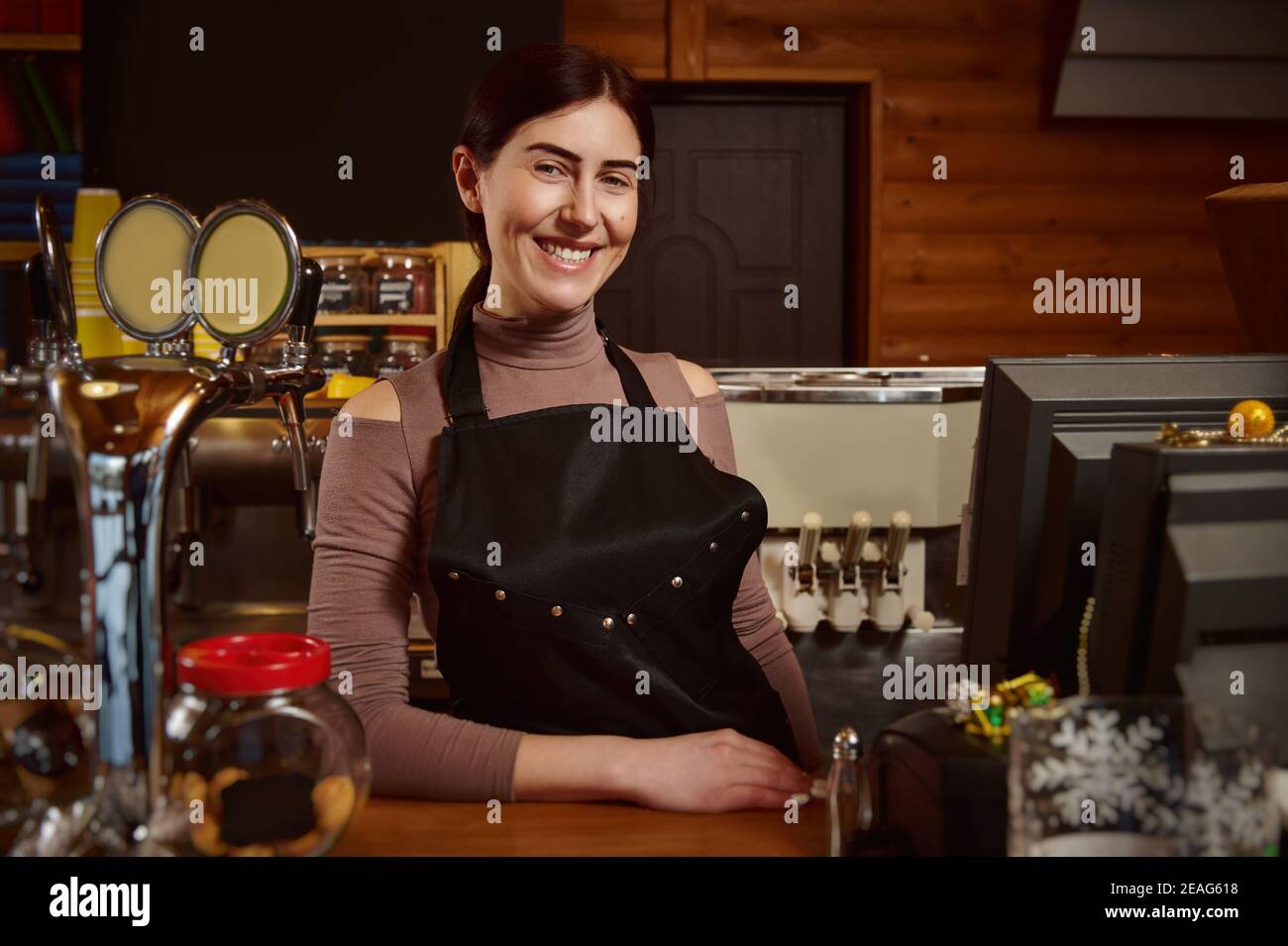 Young attractive smiling female barista in apron standing behind the ...