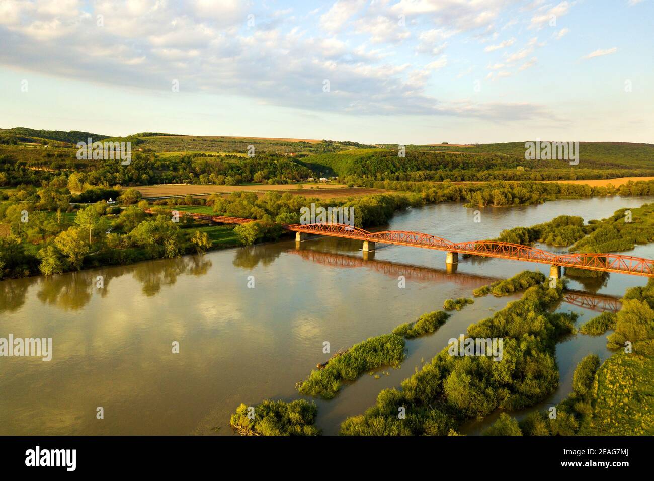 Aerial view of a narrow road bridge stretching over muddy wide river in ...