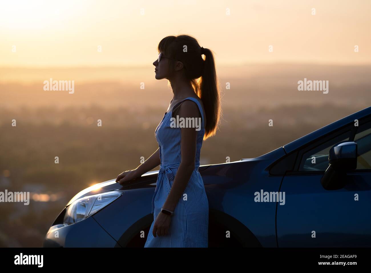 Young female driver resting near her car enjoying warm summer evening ...