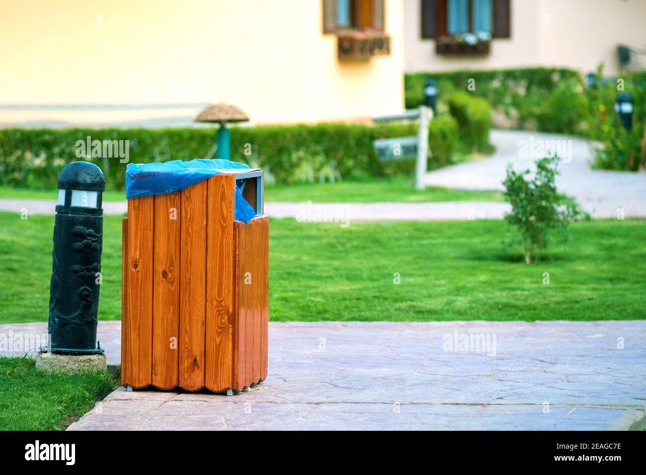 Yellow wooden trash can outdoors on the side of sidewalk in park ...