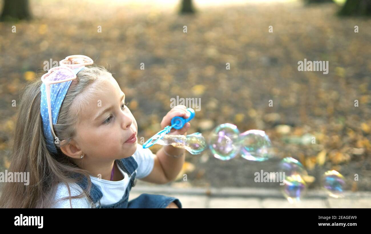 Little happy child girl blowing soap bubbles outside in green park ...