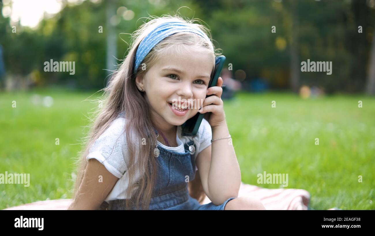 Positive little child girl having conversation on her mobile phone in ...