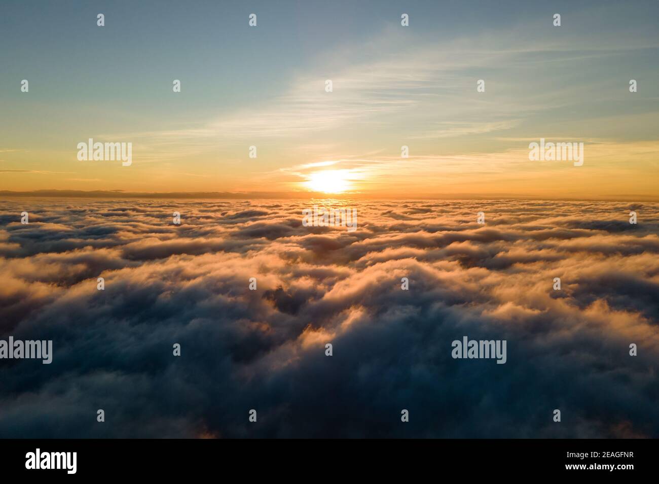 Aerial view of vibrant yellow sunrise over white dense clouds with blue ...