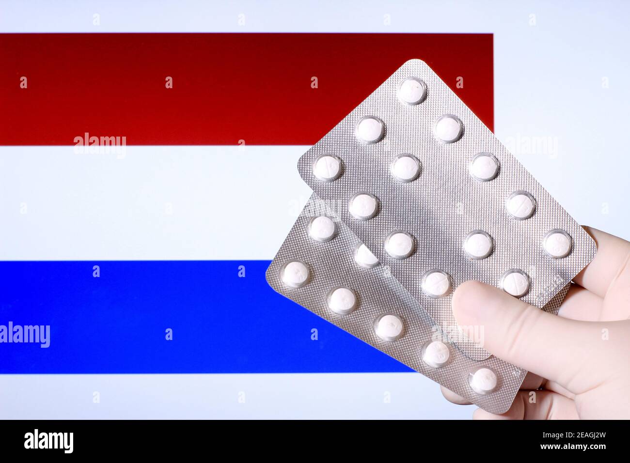 Hand in surgical glove holding pill blisters. Dutch flag in the ...