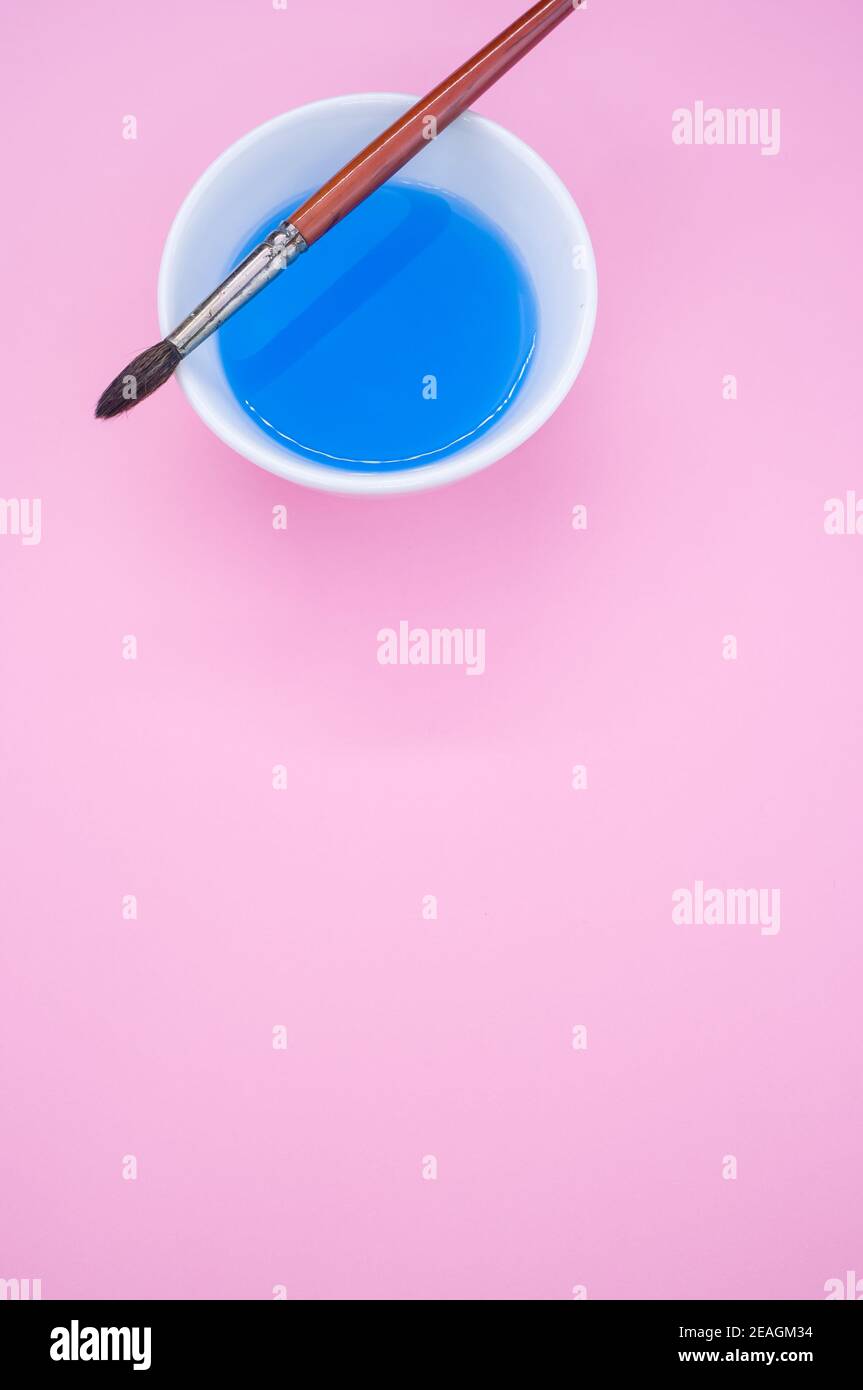 Vertical shot of blue liquid watercolor paint on a bowl and paintbrush ...