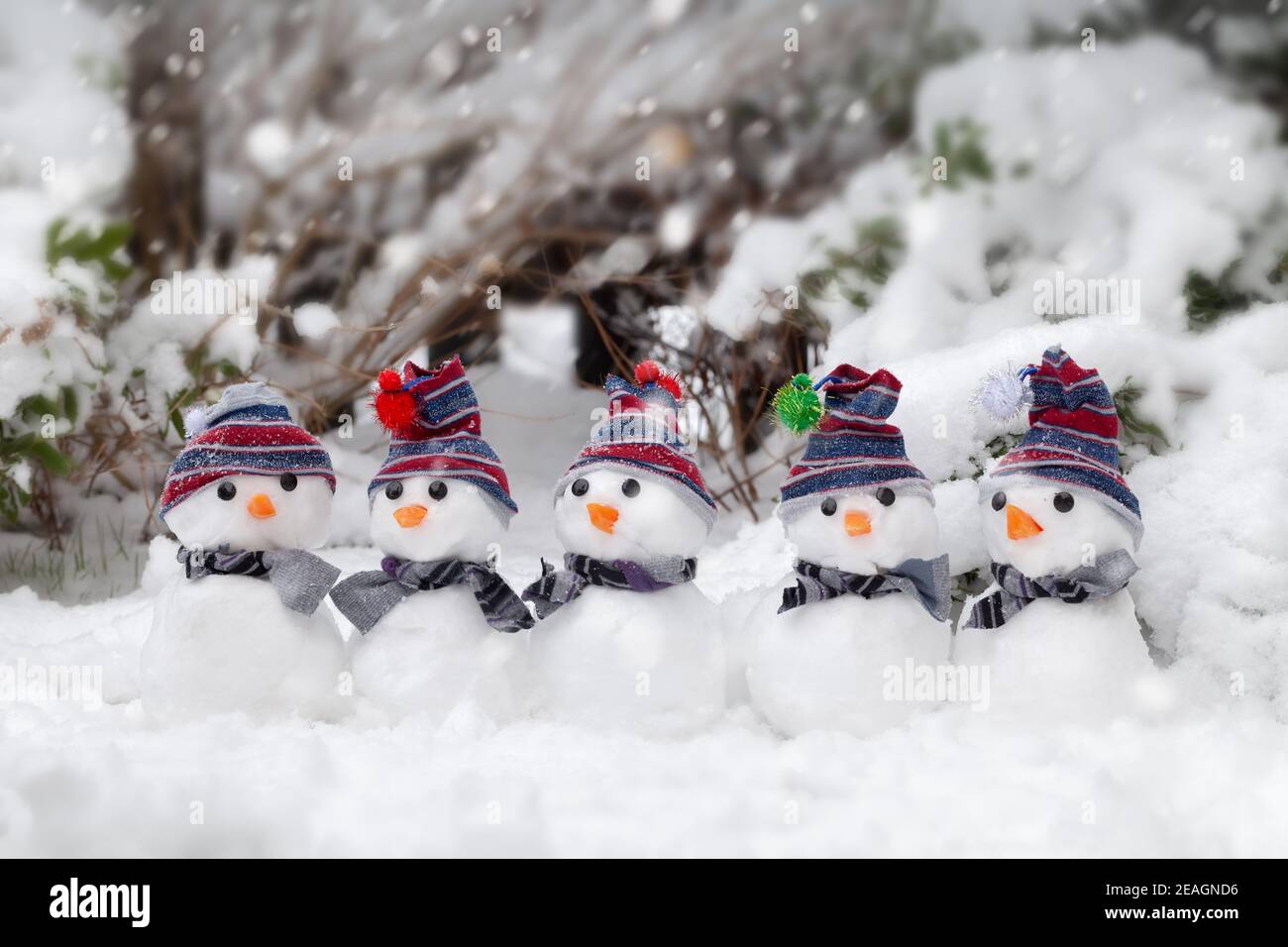 Five little cute snowmen dressed in hats and scarfs sat in the snow in ...