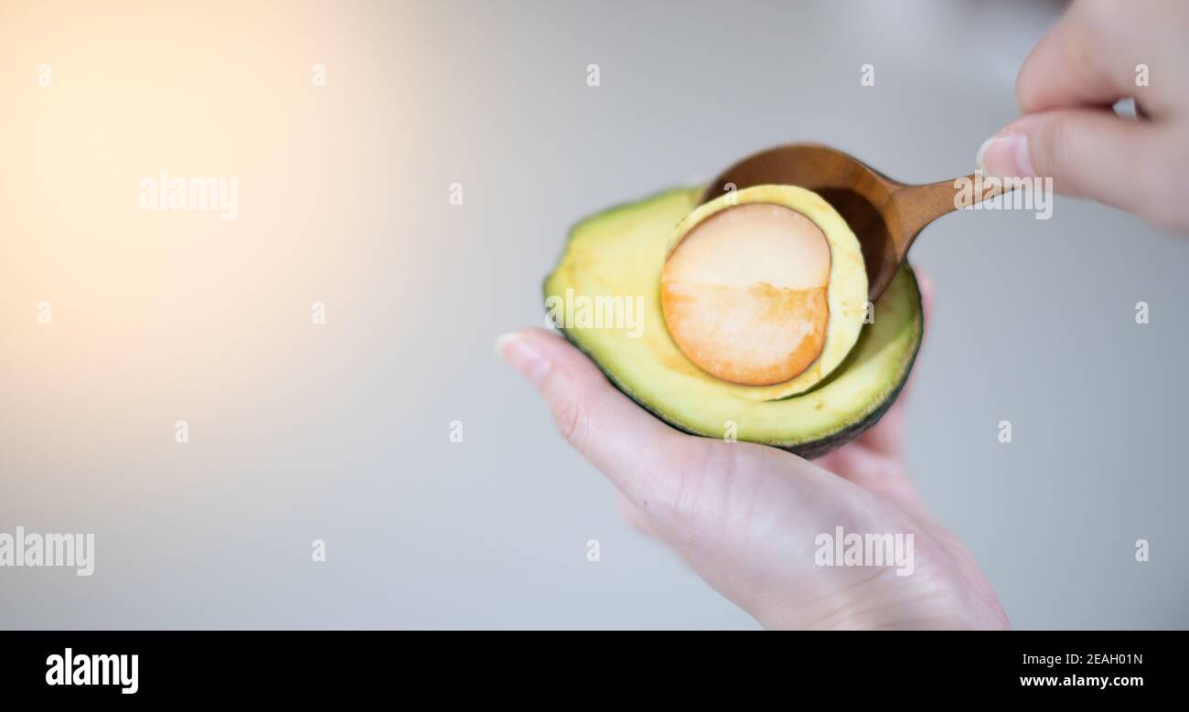 Female hand using a spoon to scoop the avocado out of the shell and ...