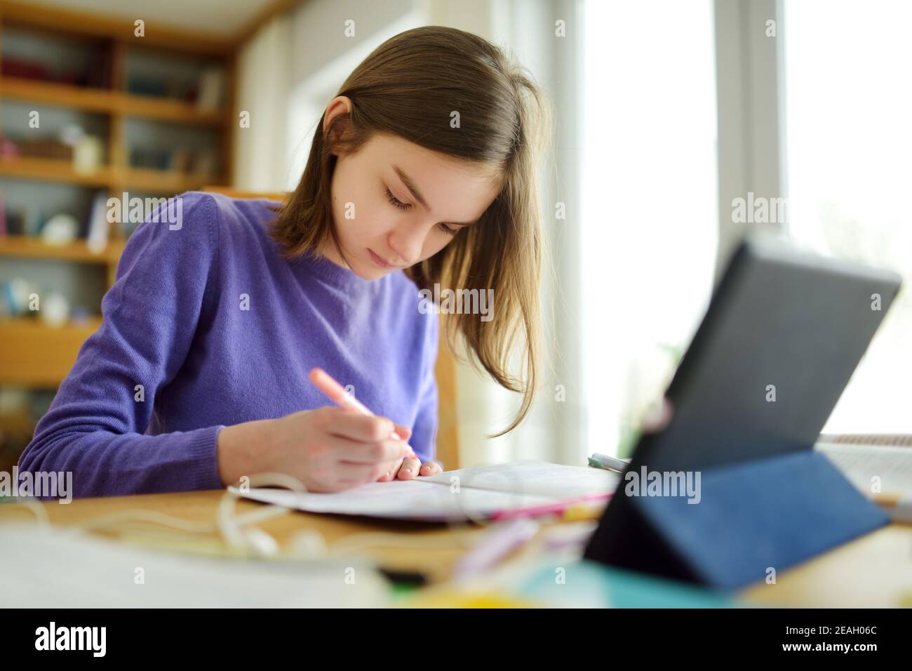 Preteen schoolgirl doing her homework with digital tablet at home ...