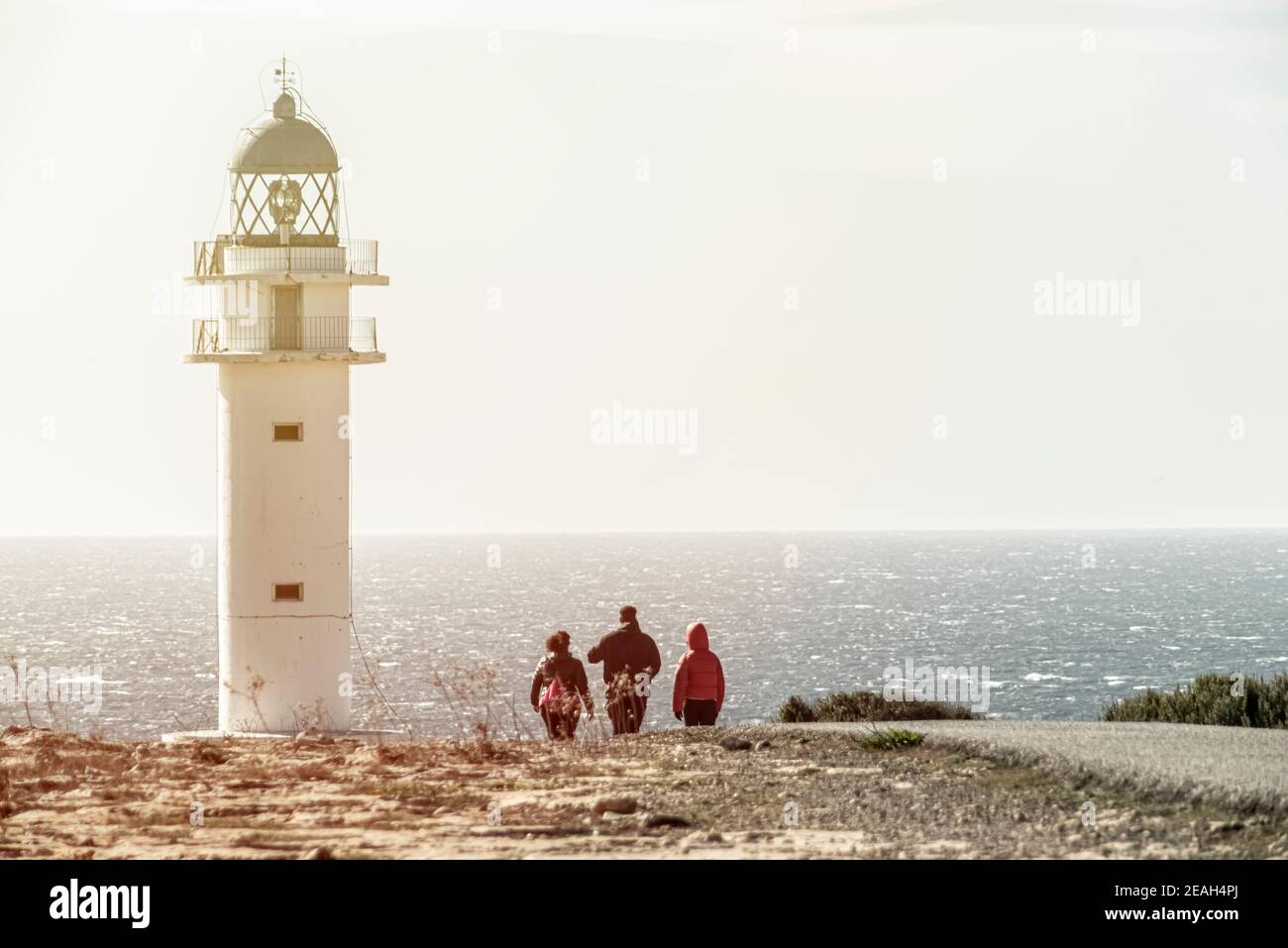Three people walking towards a lighthouse in the sea at sunset Stock ...