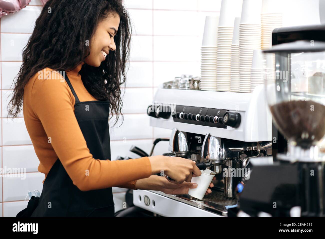 An African American smiling female professional barista makes coffee ...