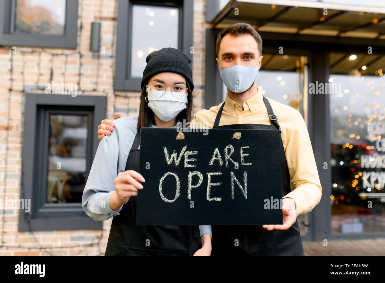 Welcome, we are OPEN. Two friendly waiters wearing protective masks ...