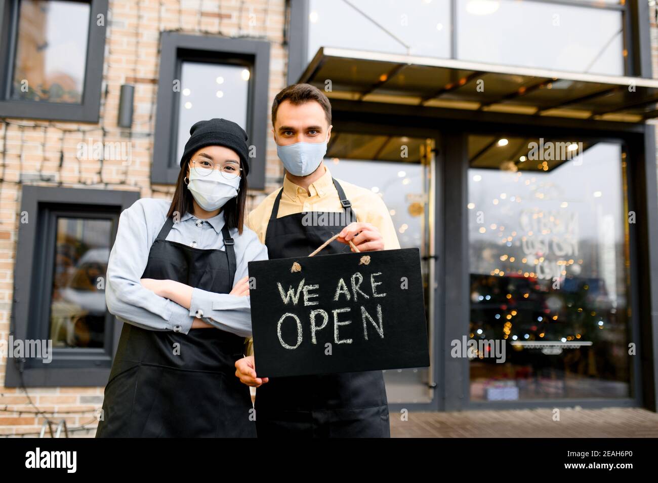 Welcome, we are OPEN. Two friendly waiters wearing protective masks ...