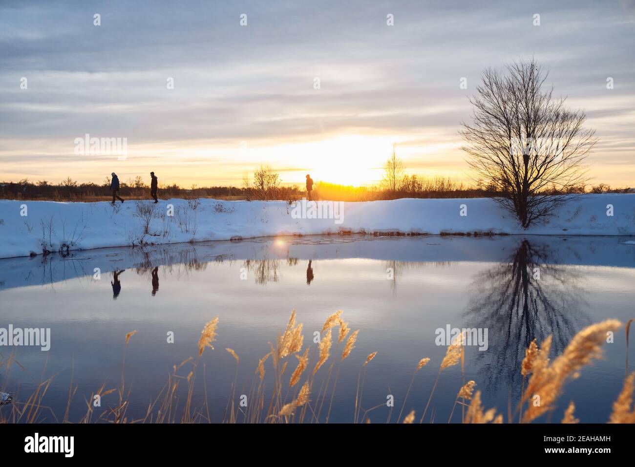 Silhouettes of three people are reflected in the blue water of a ...