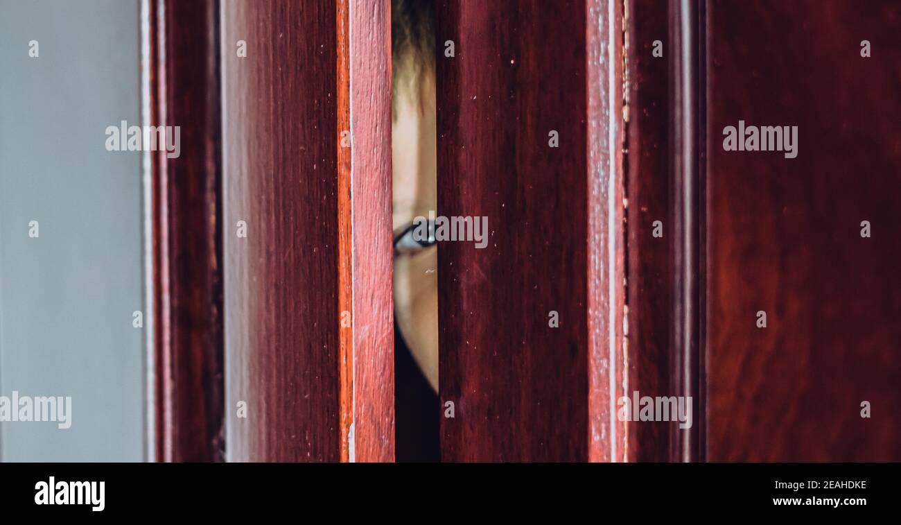 Sad boy hide in closet, close-up view of blue eye in ajar door slit ...