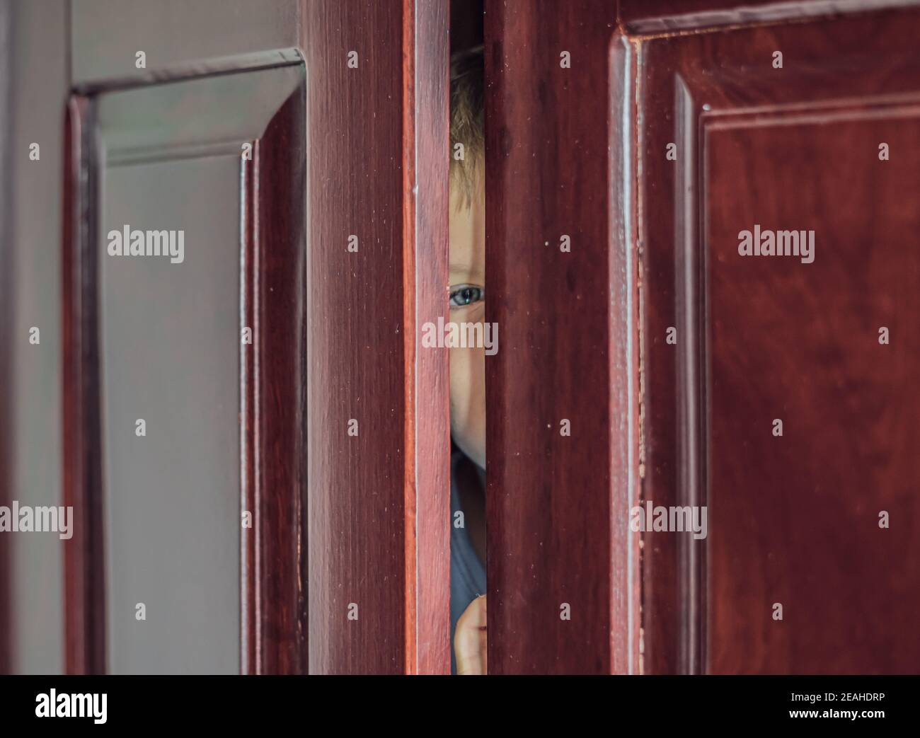 Sad boy hide in closet, close-up view of blue eye in ajar door slit ...