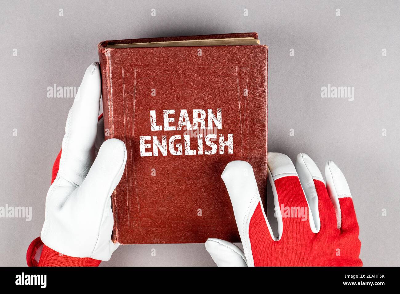 Learn English concept. Leather work gloves in hand and a textbook on a ...