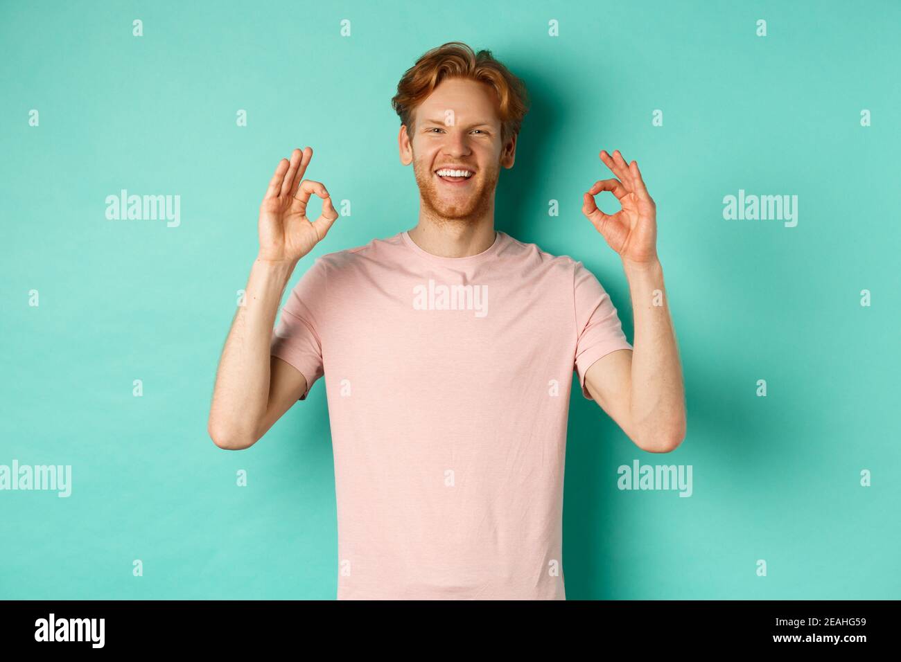 Attractive young man in t-shirt smiling satisfied, nod in approval and ...