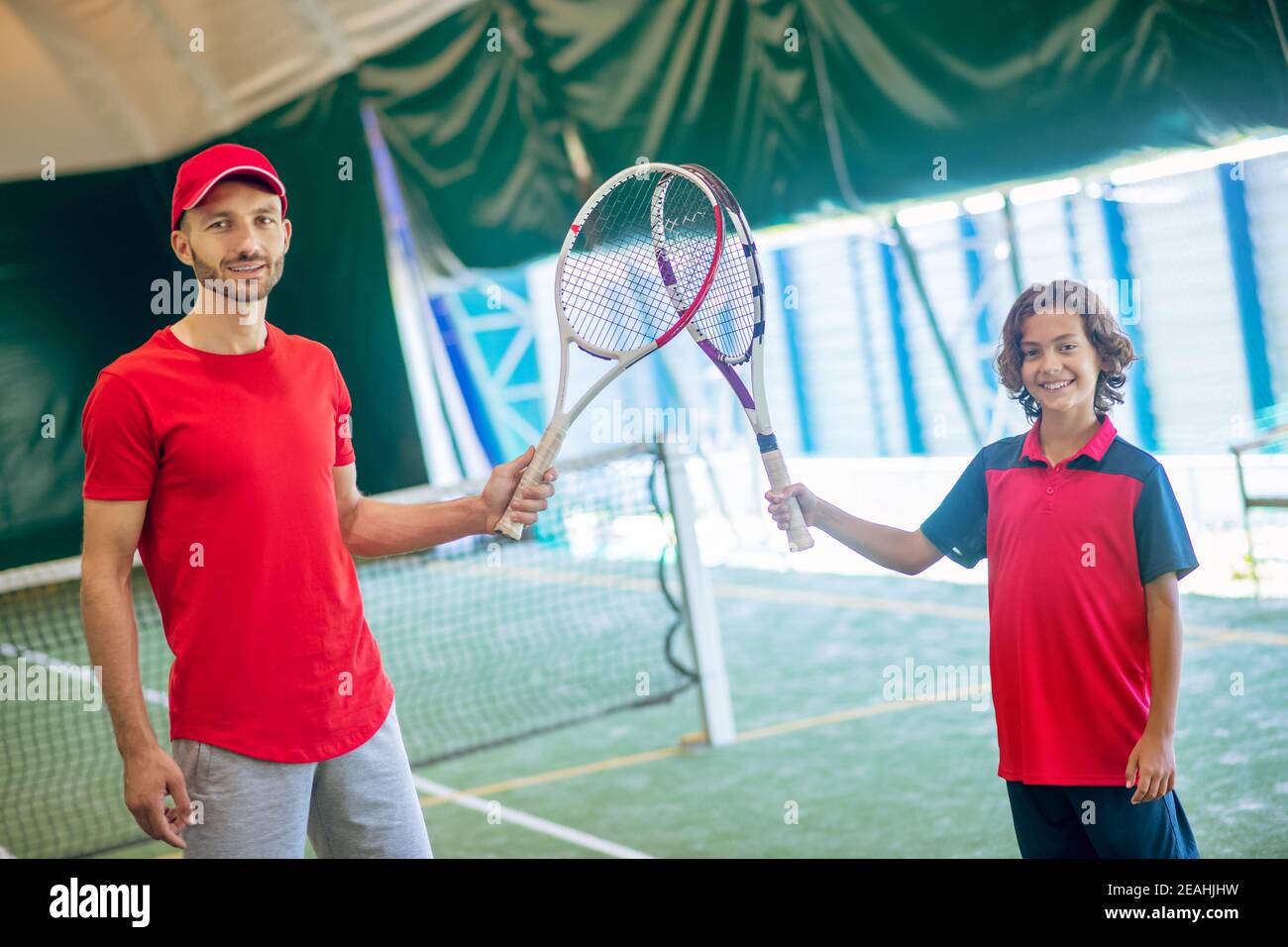 Coach in a red cap and a boy holding tennis rackets in hands Stock ...