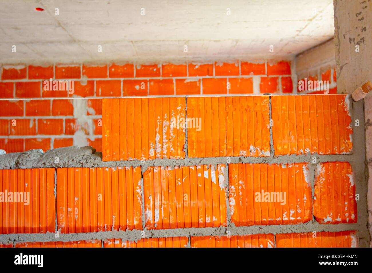 Mason, bricklayer worker is using red blocks to mount a wall next the ...