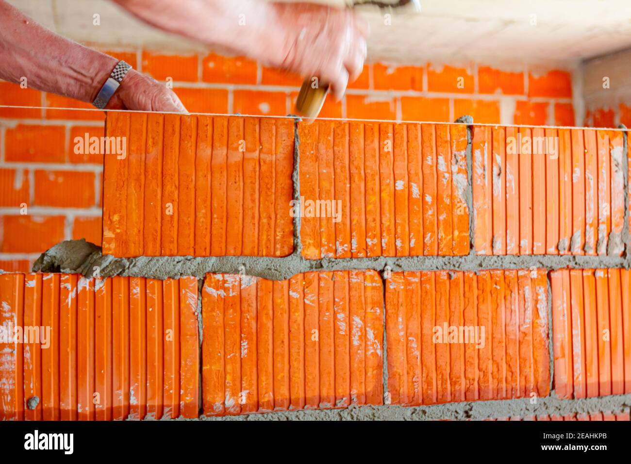 Mason, bricklayer worker is using red blocks to mount a wall next the ...