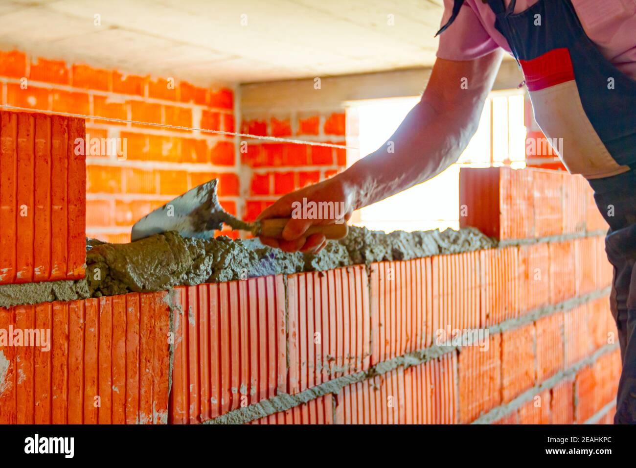 Worker is using spatula, trowel, to apply mortar on red blocks to make ...