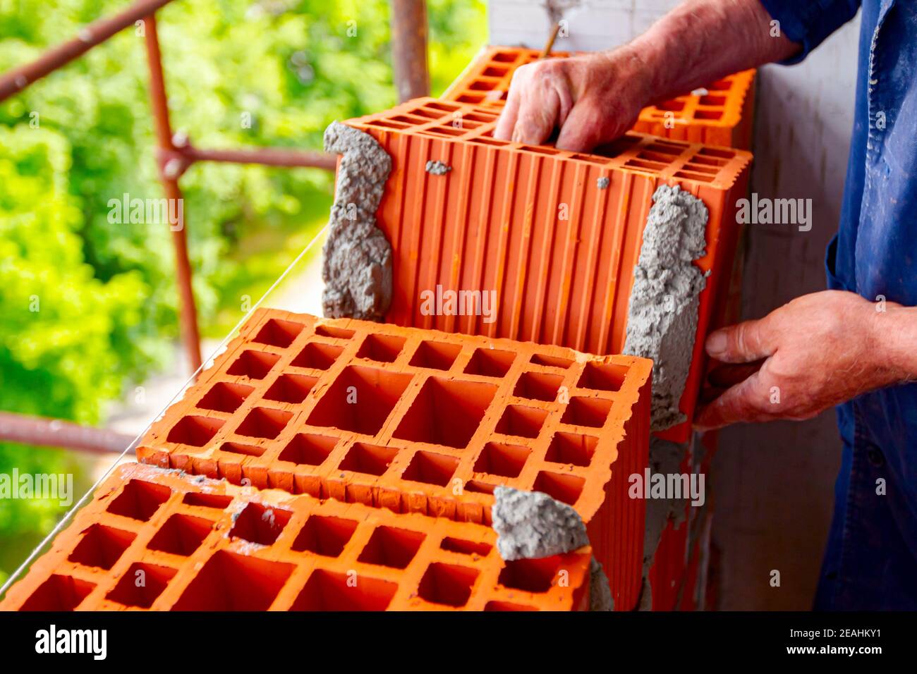 Mason, bricklayer worker is using red blocks to mount a wall next the ...