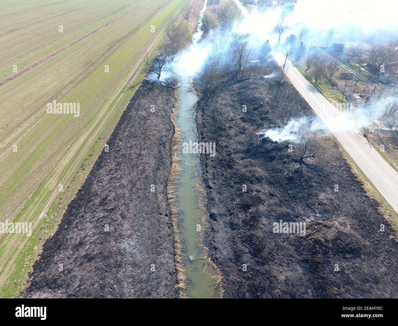 Burning dry grass along the irrigation canal. Smoke and the flame of ...